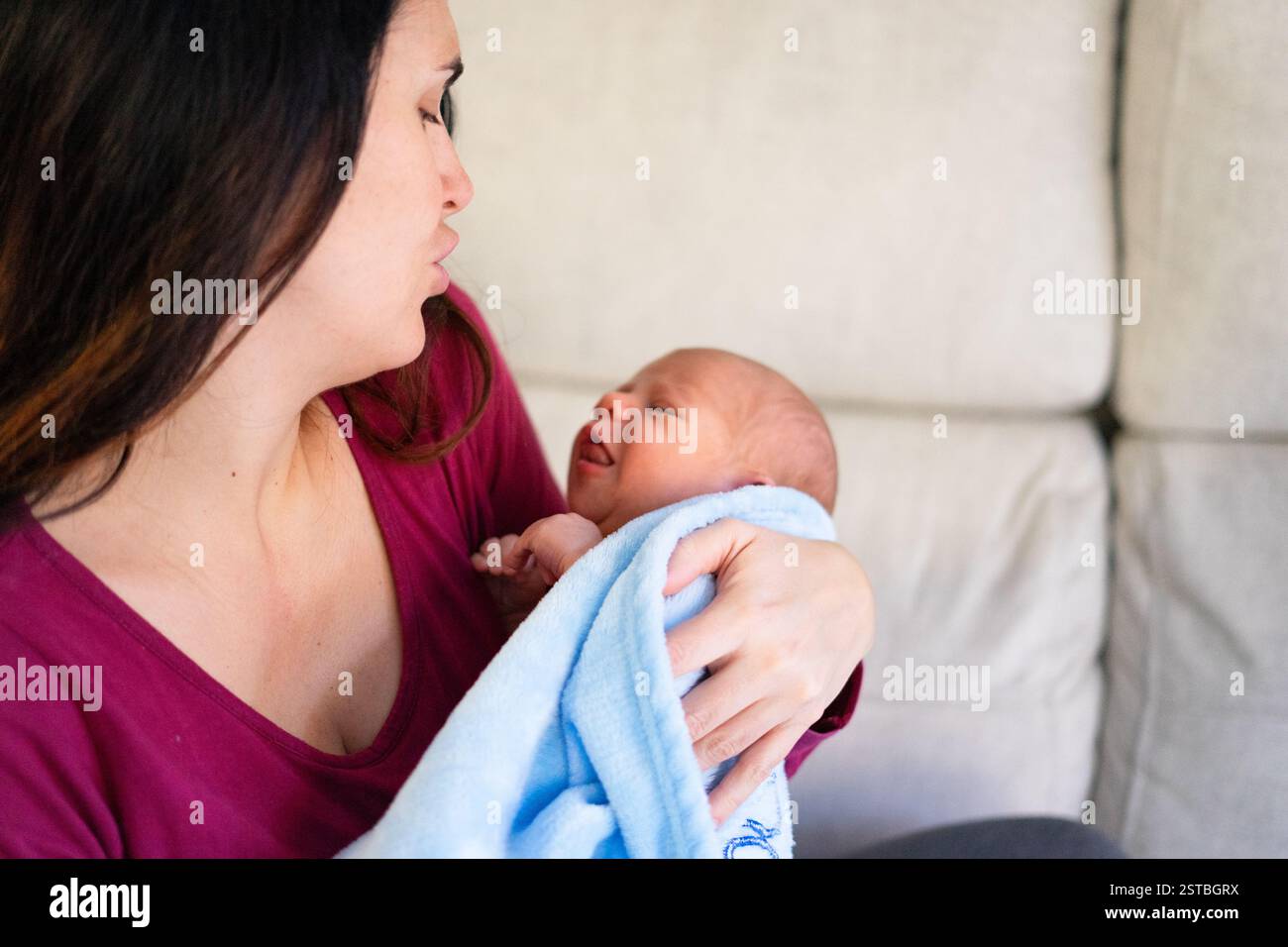 Mother comforting her crying newborn baby wrapped in a blue blanket, showing the challenges and ...