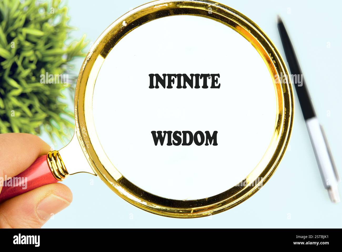 A hand holding a magnifying glass focuses on the words infinite wisdom, symbolizing the search ...