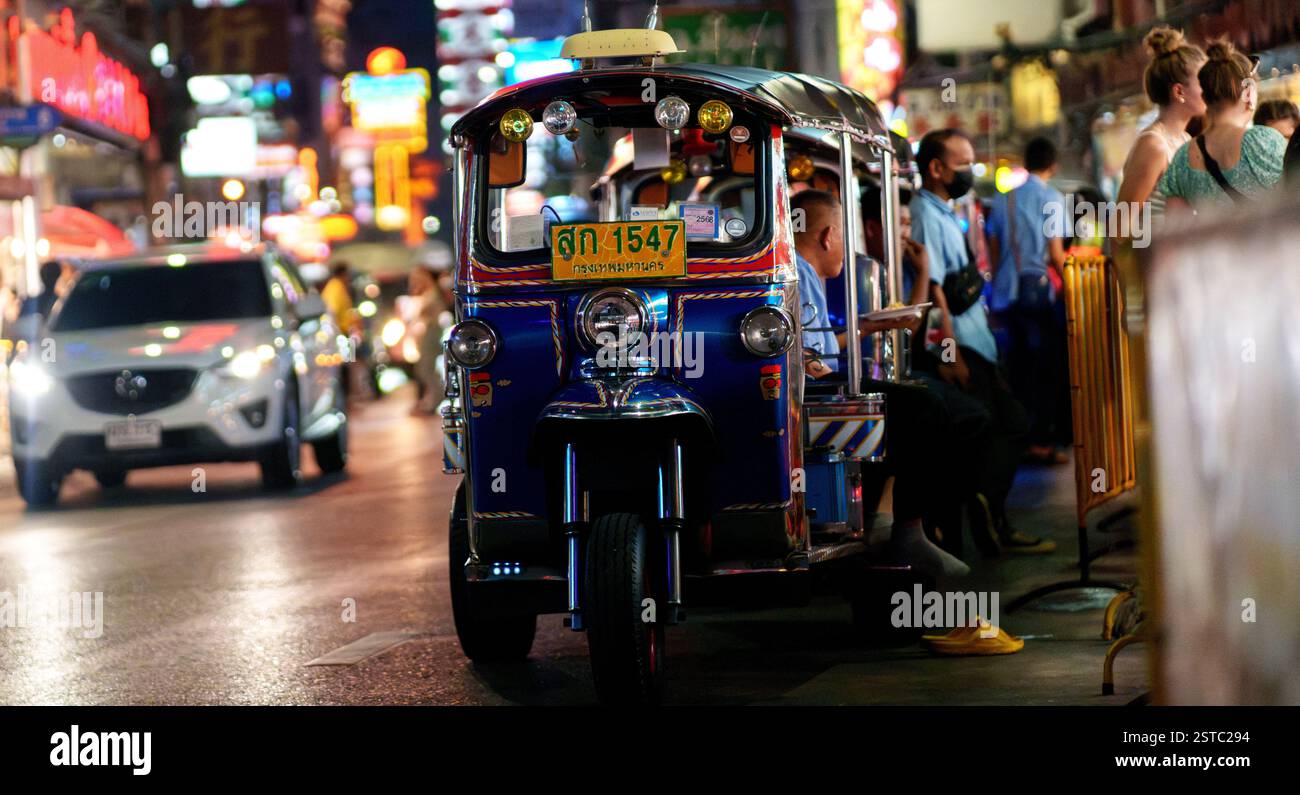 A vibrant night scene in Bangkok's Chinatown with a traditional tuk-tuk prominently featured in ...