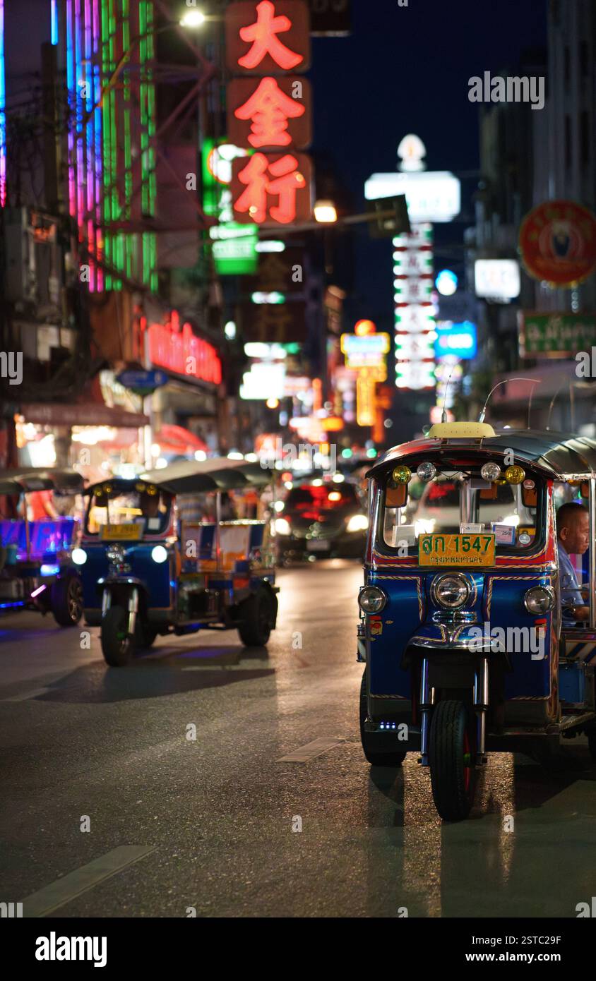 Nighttime scene in Bangkok's Chinatown featuring iconic tuk-tuks navigating through the vibrant ...