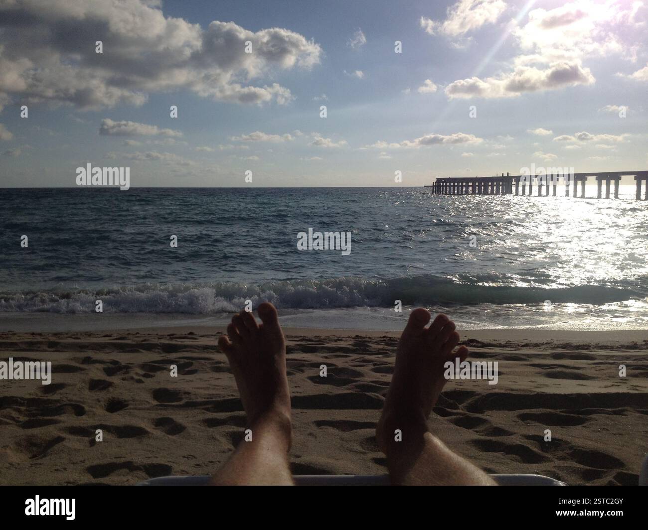 Man relaxing on Miami beach, feet in sand, pier in background. Peaceful ...
