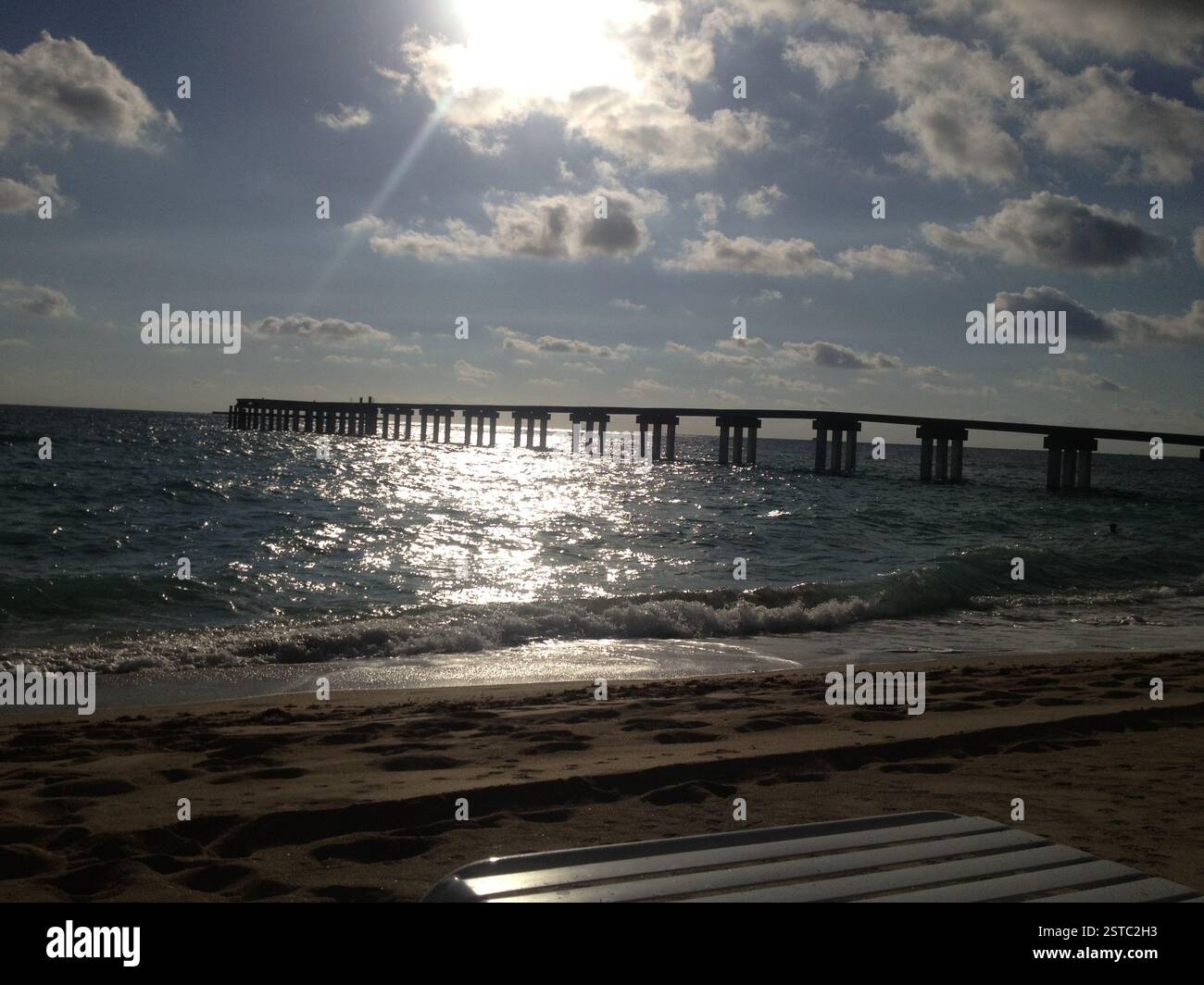 Beach pier stretching into the ocean at sunset, with waves lapping at ...