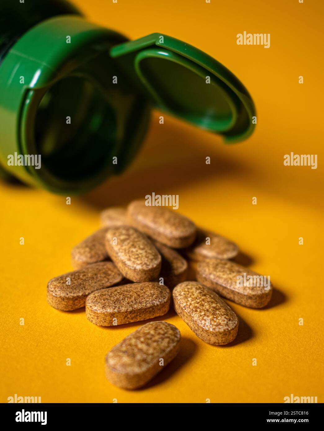 An open bottle of multivitamin tablets, pills on yellow background ...
