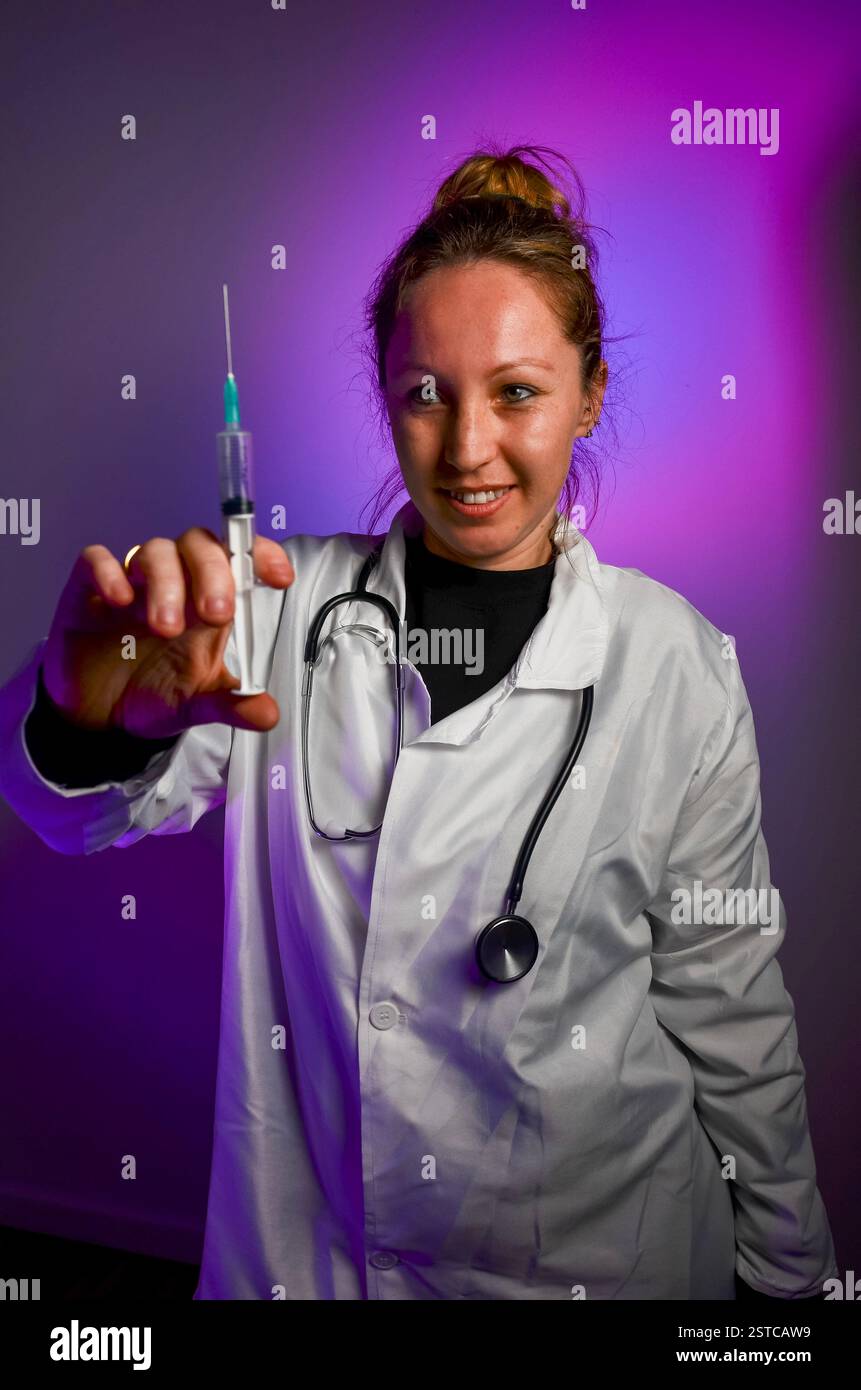 Female doctor smiles while holding a syringe, ready to administer an ...