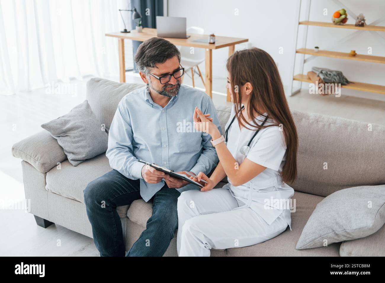 Female doctor is sitting with mature customer on the sofa. Professional ...
