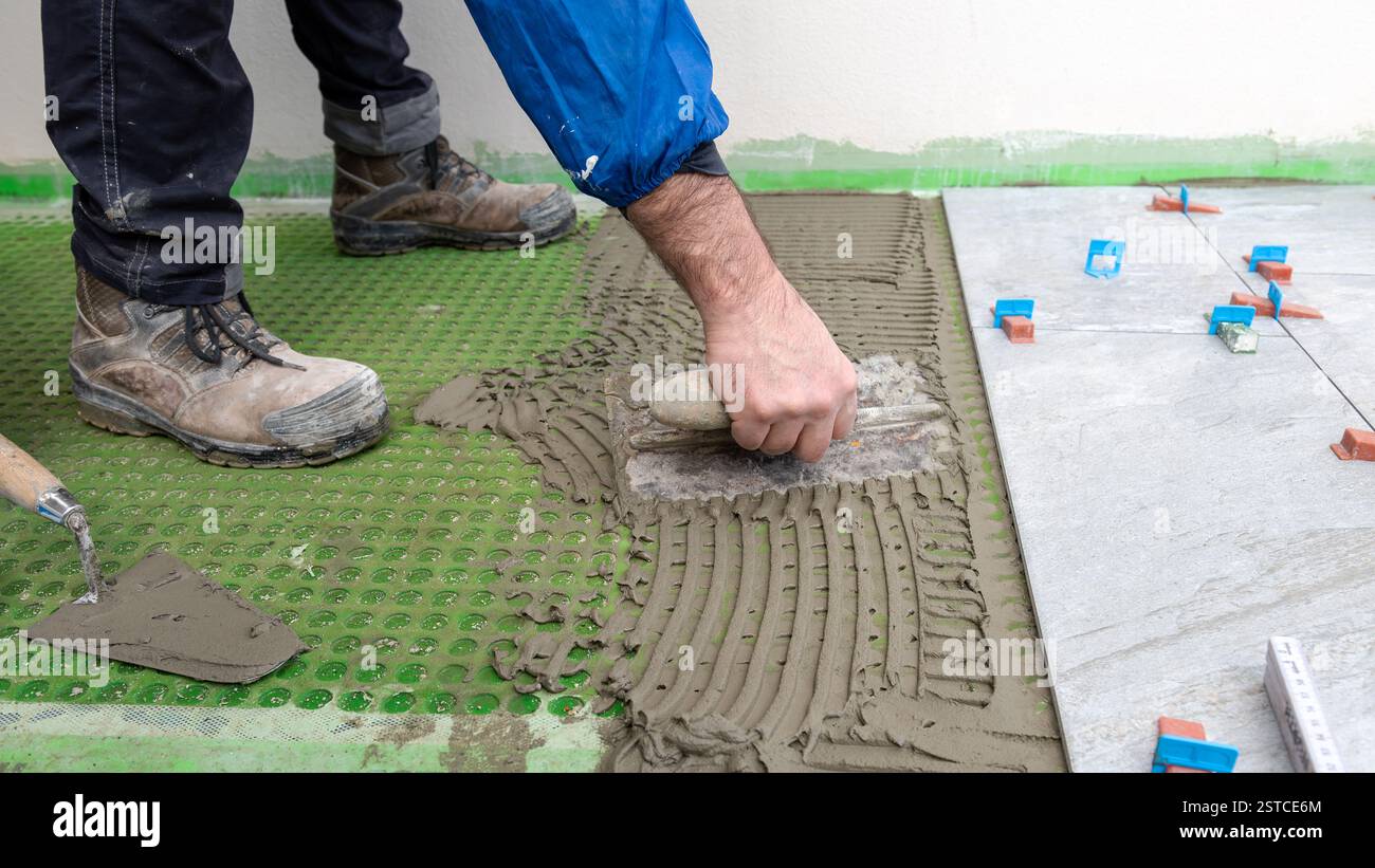 Bricklayer tiler spreads glue with notched trowel to install tiles for ...