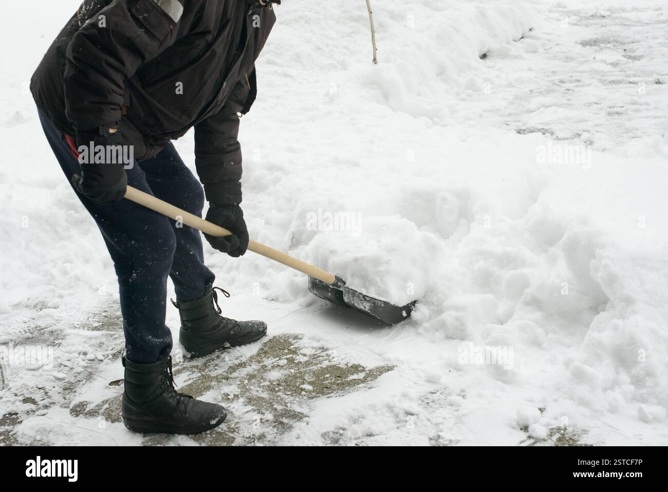 A person bundled in winter clothing shovels thick snow from a sidewalk ...