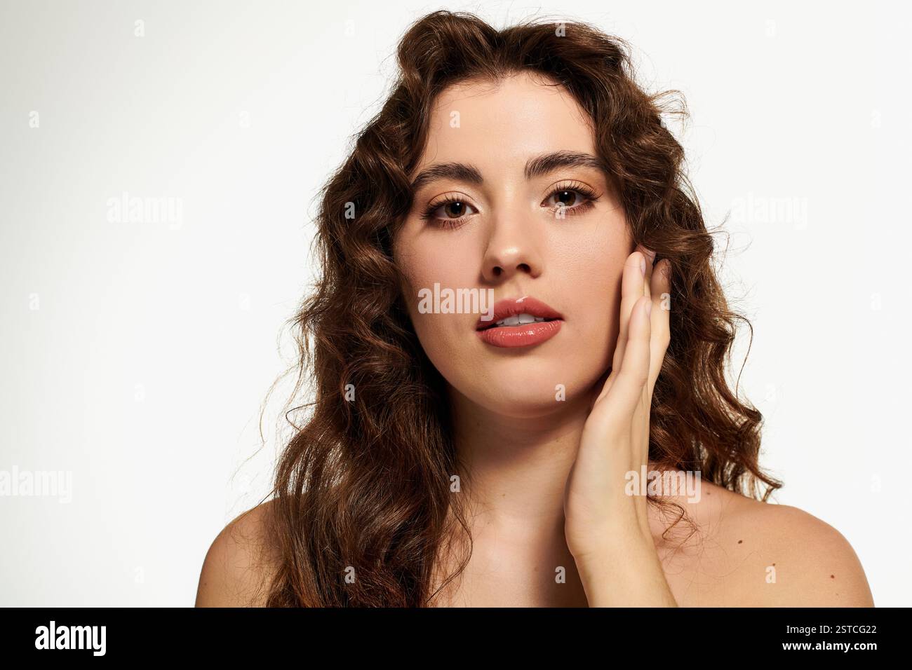 Charming young woman with beautiful curls gently touching her face in a ...