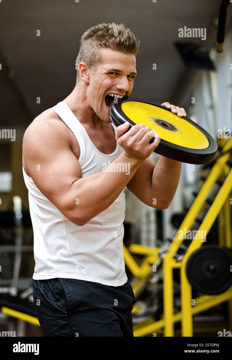 Handsome young man biting big weight disc in gym hi-res stock ...