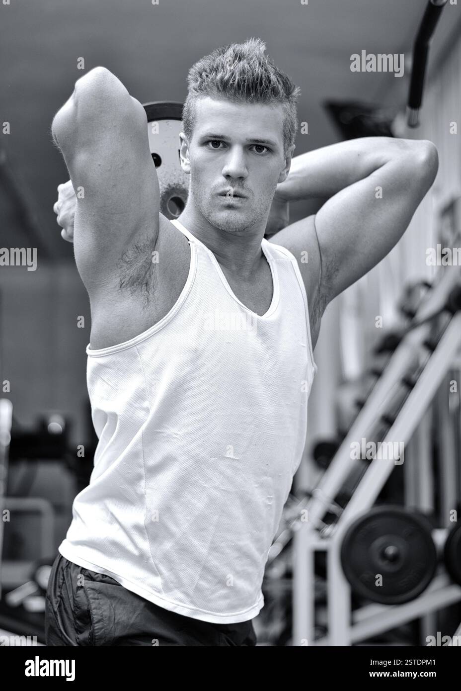 Attractive young man training triceps, lifting weight over his head ...