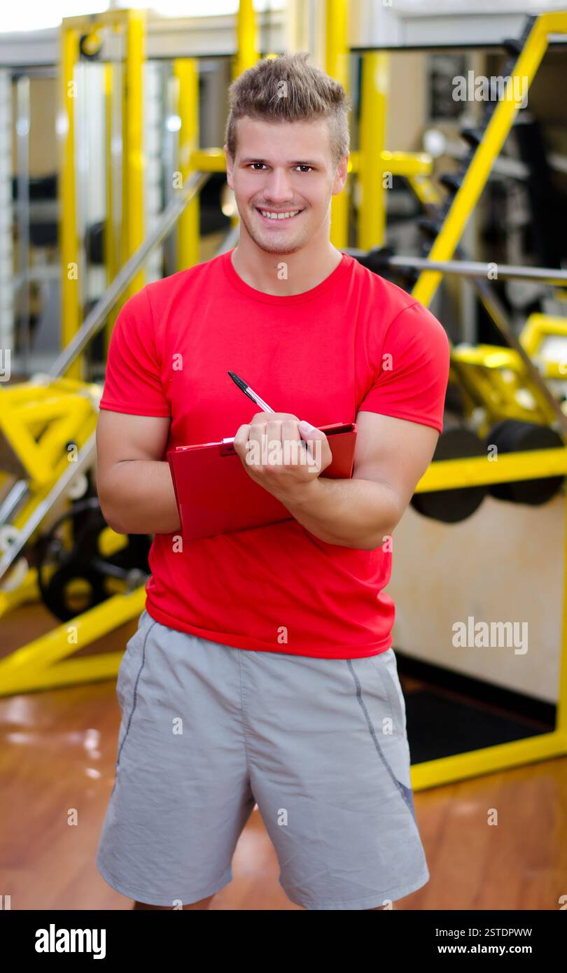 Young male personal trainer writing on clipboard, with training ...