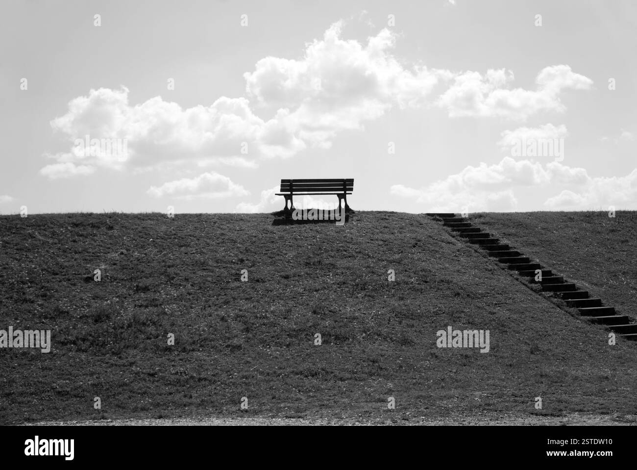 Bench on an embankment with steps in front of a blue and white cloudy ...