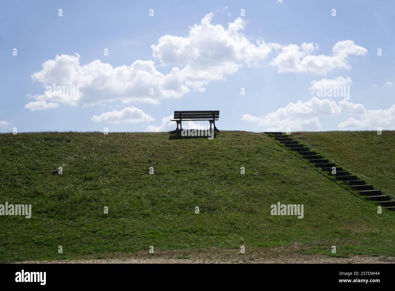 Bench on an embankment with steps in front of a blue and white cloudy ...