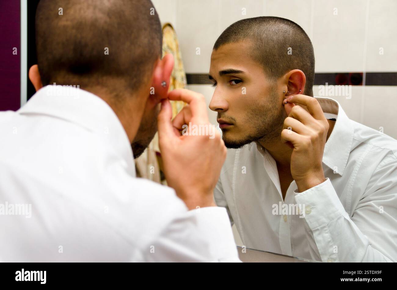 Handsome young man touching and examining his ear piercings Stock Photo ...