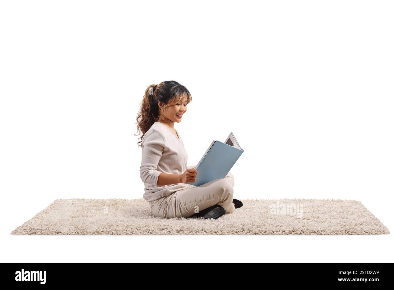 Asian woman sitting on a carpet and reading a book isolated on white ...