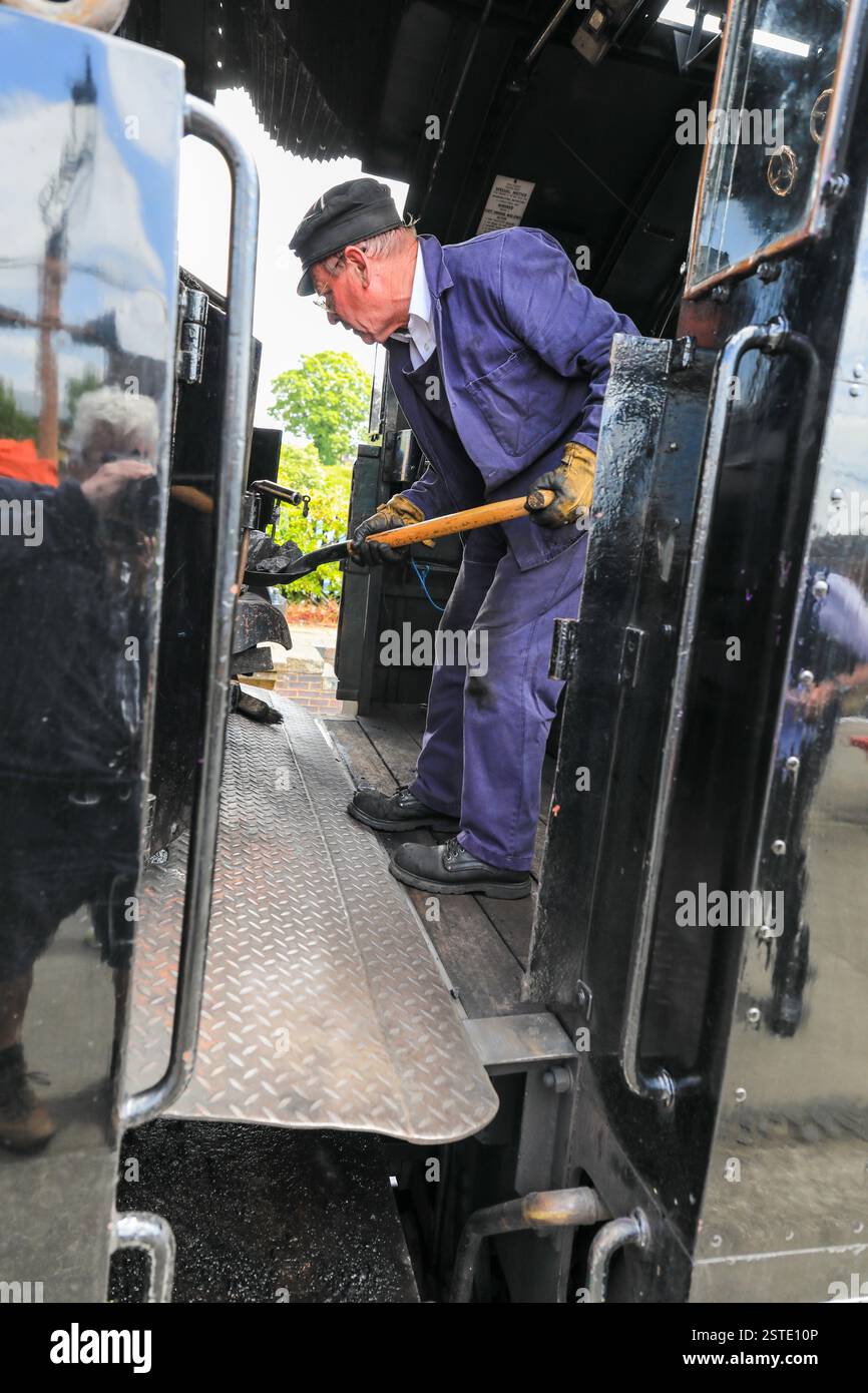 An elderly fireman on the footplate stoking the fire on a steam engine ...