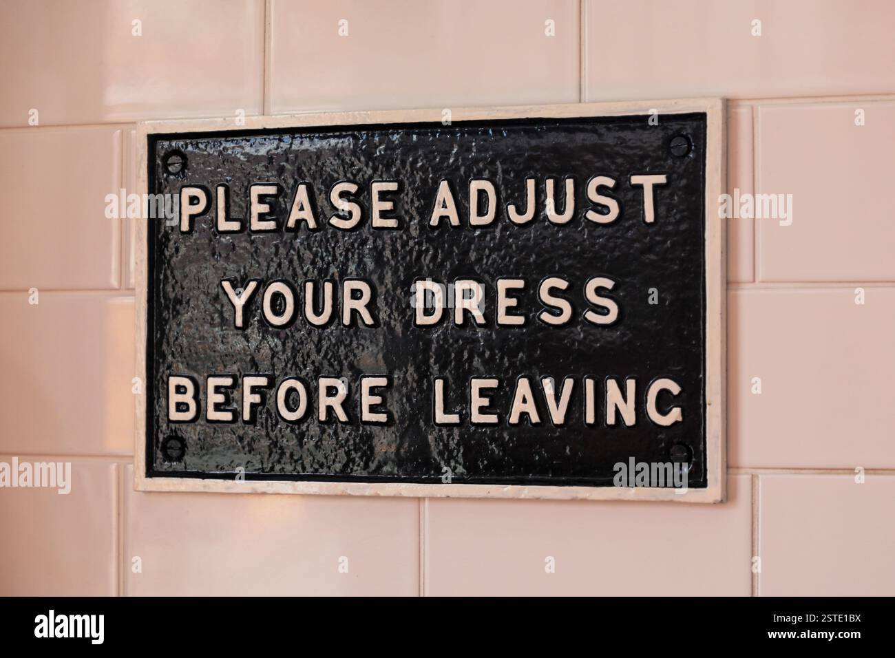 An old cast iron sign in a gents public toilet saying "Please adjust ...
