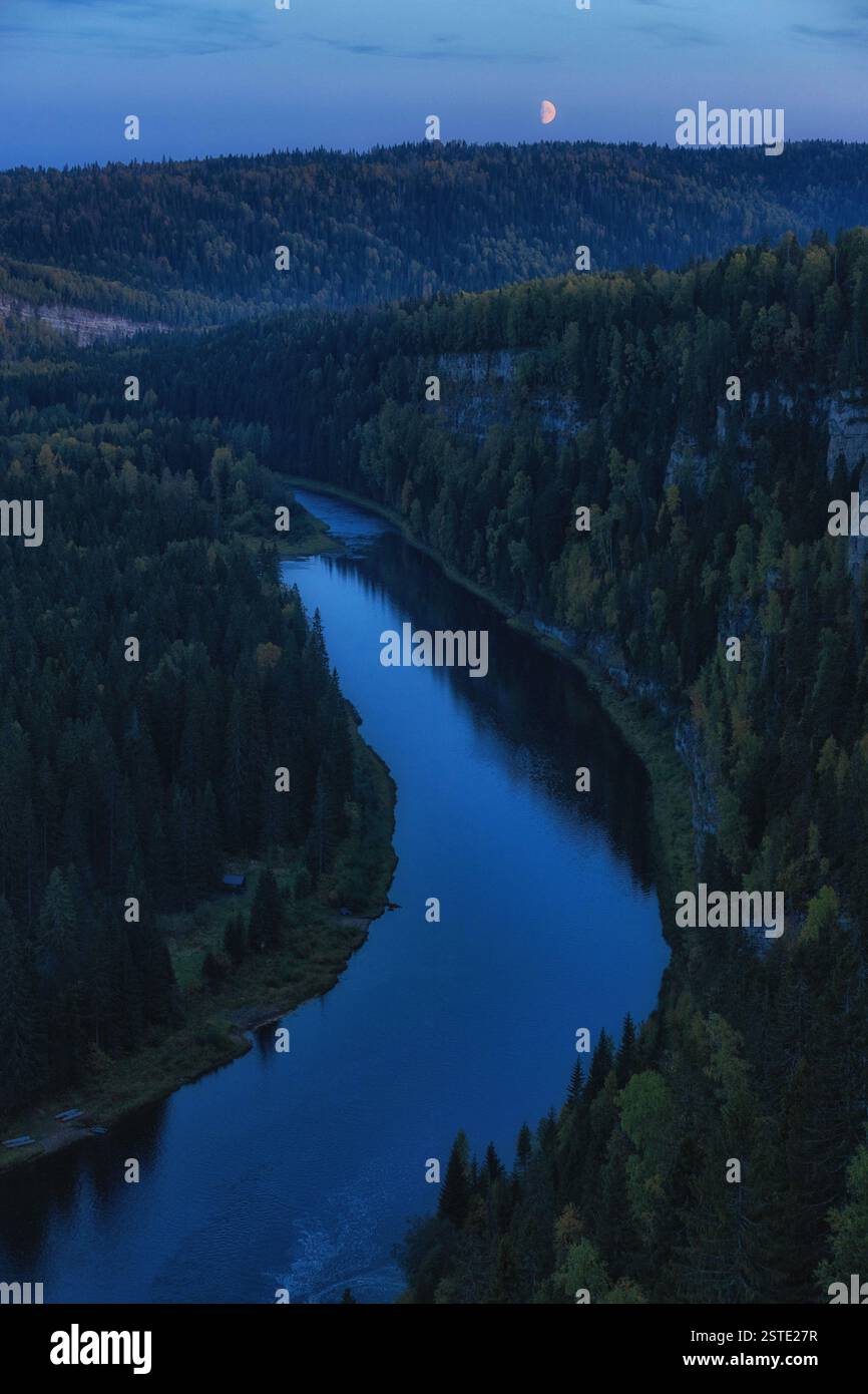 As daylight fades, a tranquil river winds through dense forests under a ...