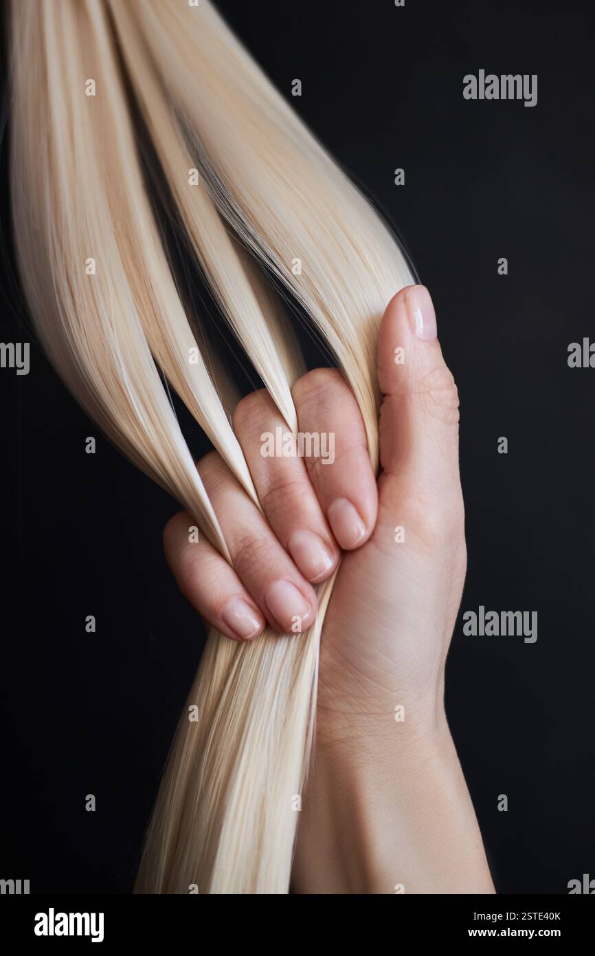 hand gently grips a long, straight strand of blonde hair, showcasing ...