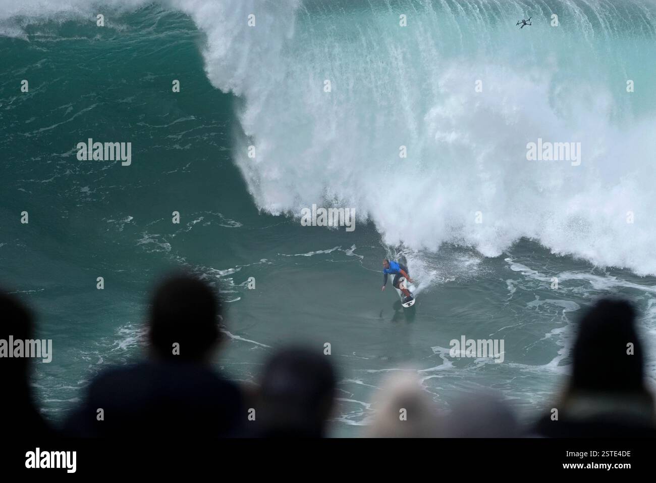 Spectators atop a cliff watch Andrew Cotton, from Britain, ride a wave ...