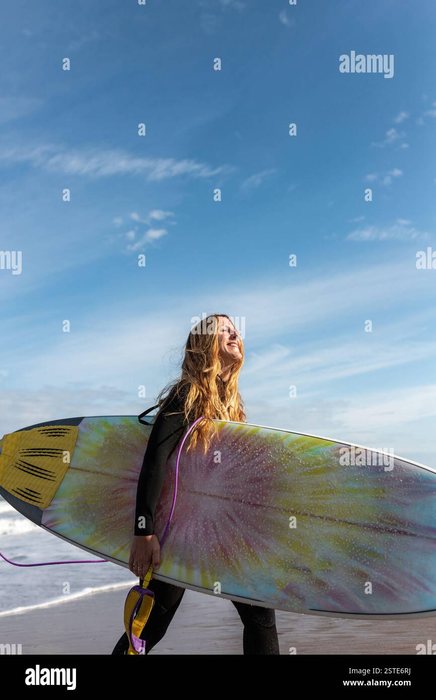 From below of sportive female surfer in black wetsuit walking on wet ...