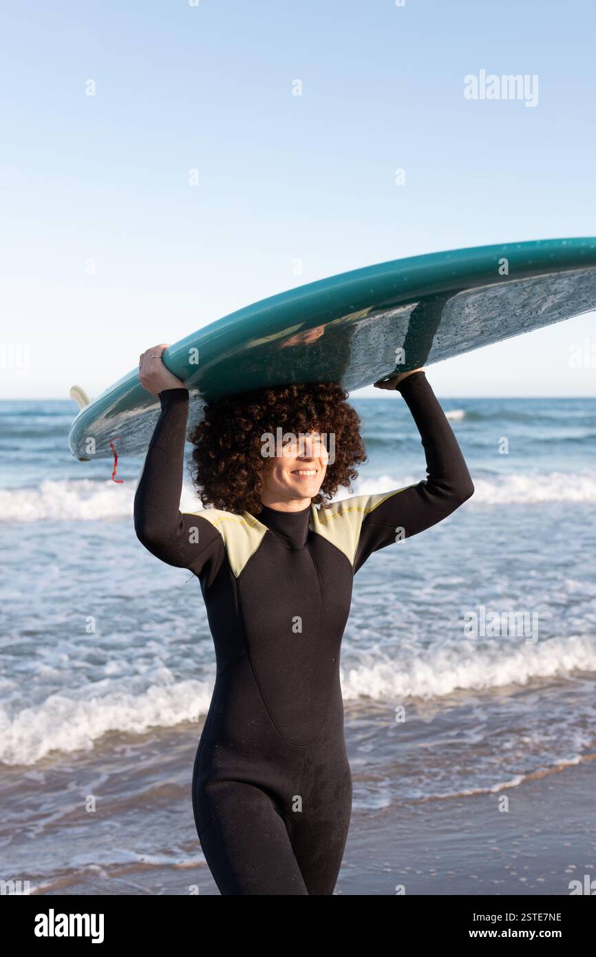 Side view of young happy female surfer in wetsuit with surfboard ...