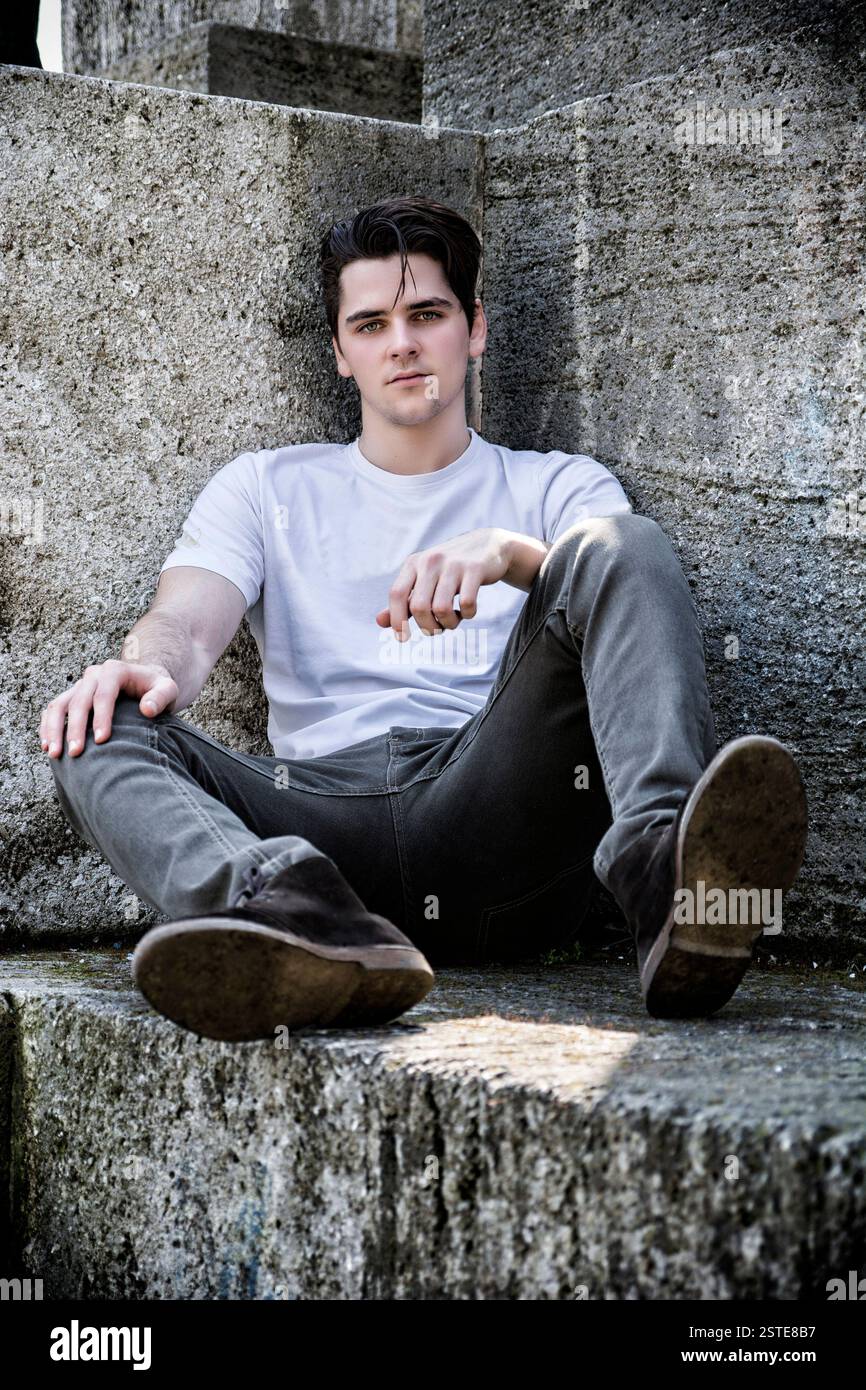 Attractive young man sitting on stone or marble blocks. Full body shot ...