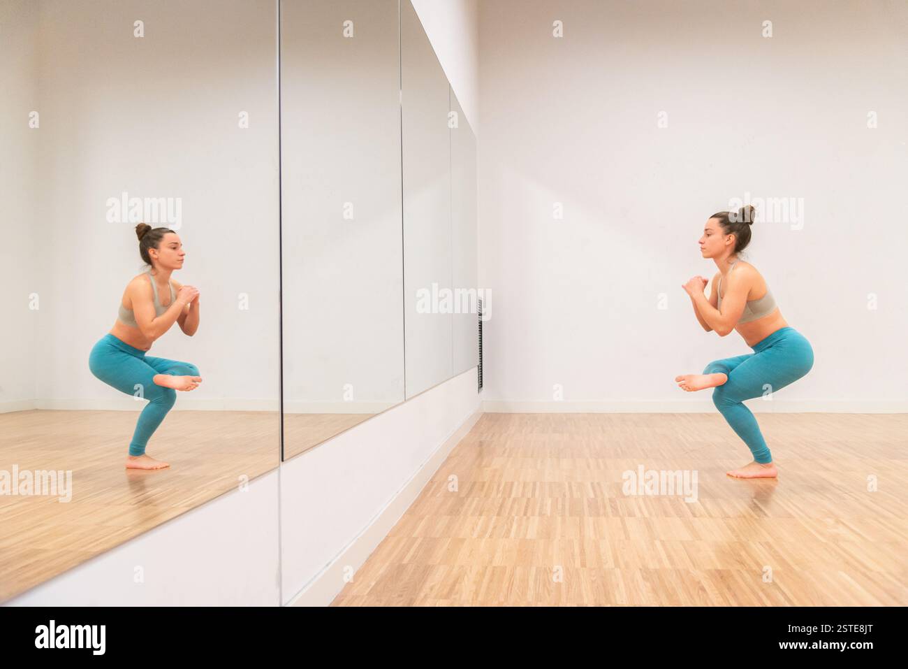 Side view of woman practicing Garland Pose (Malasana) in a yoga studio ...