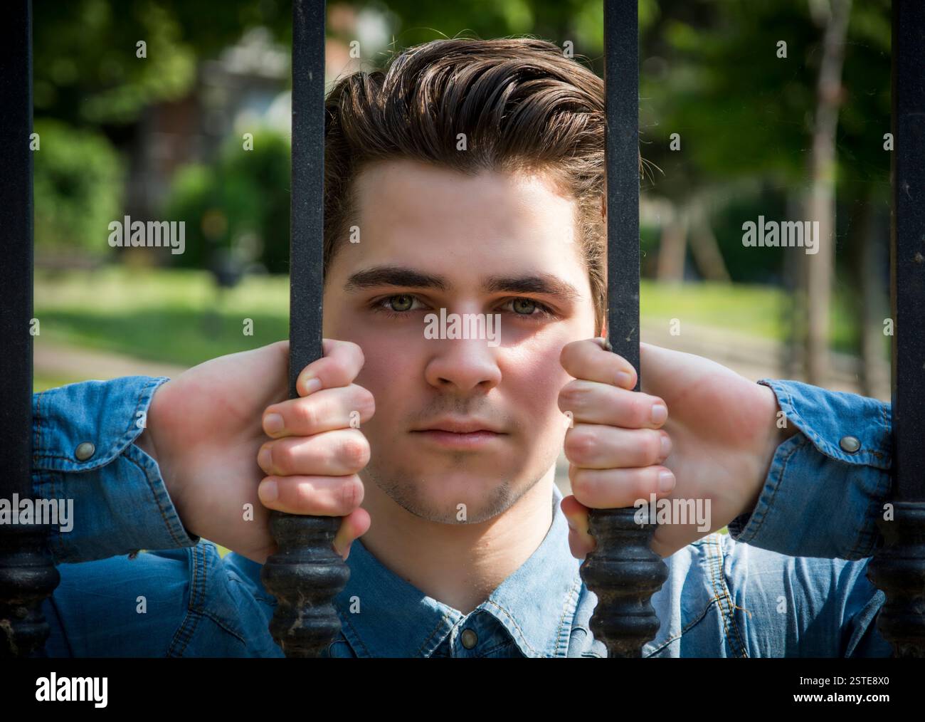 Attractive young man behind metal gate Stock Photo - Alamy