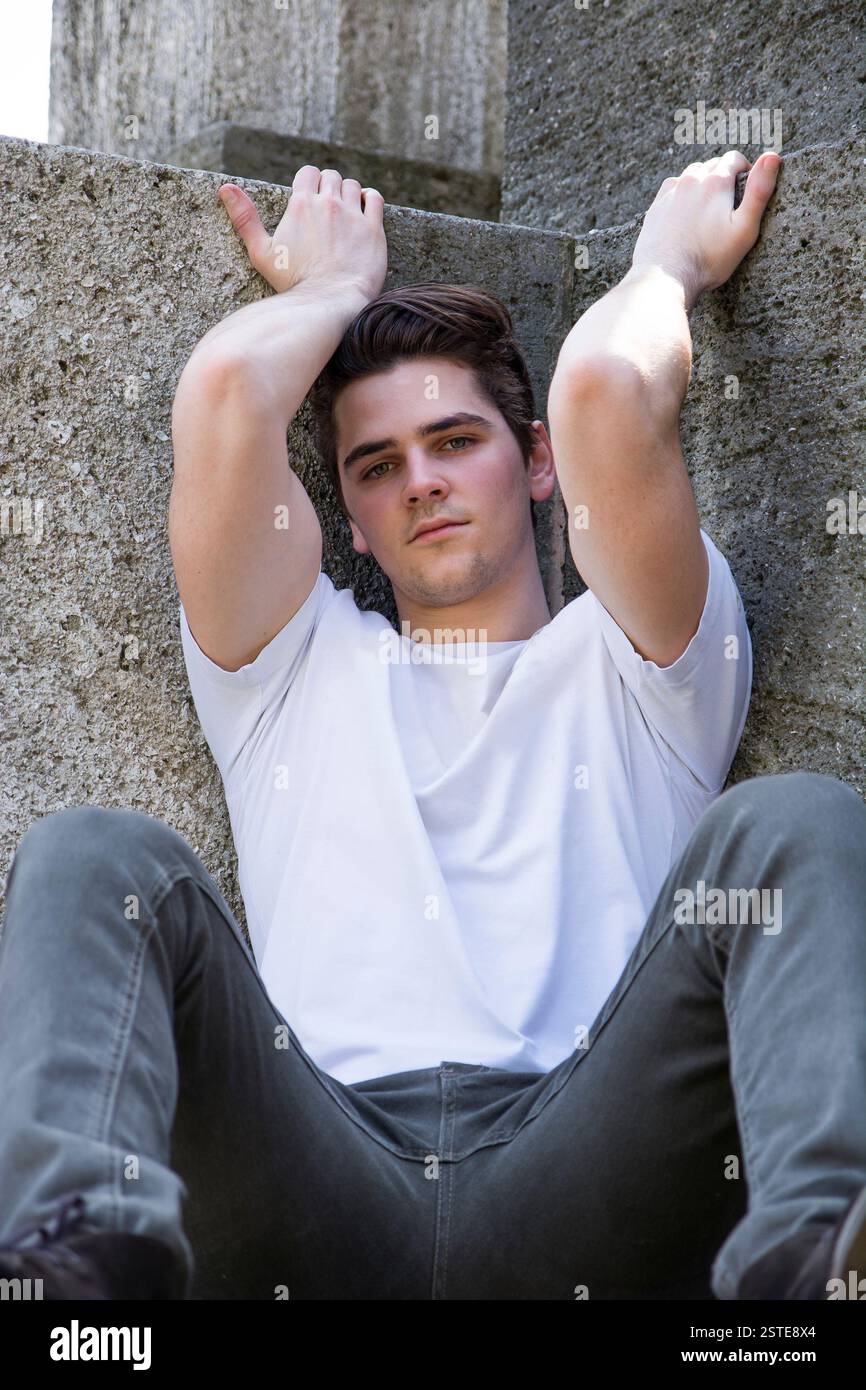 Attractive young man sitting on the ground against stone blocks ...
