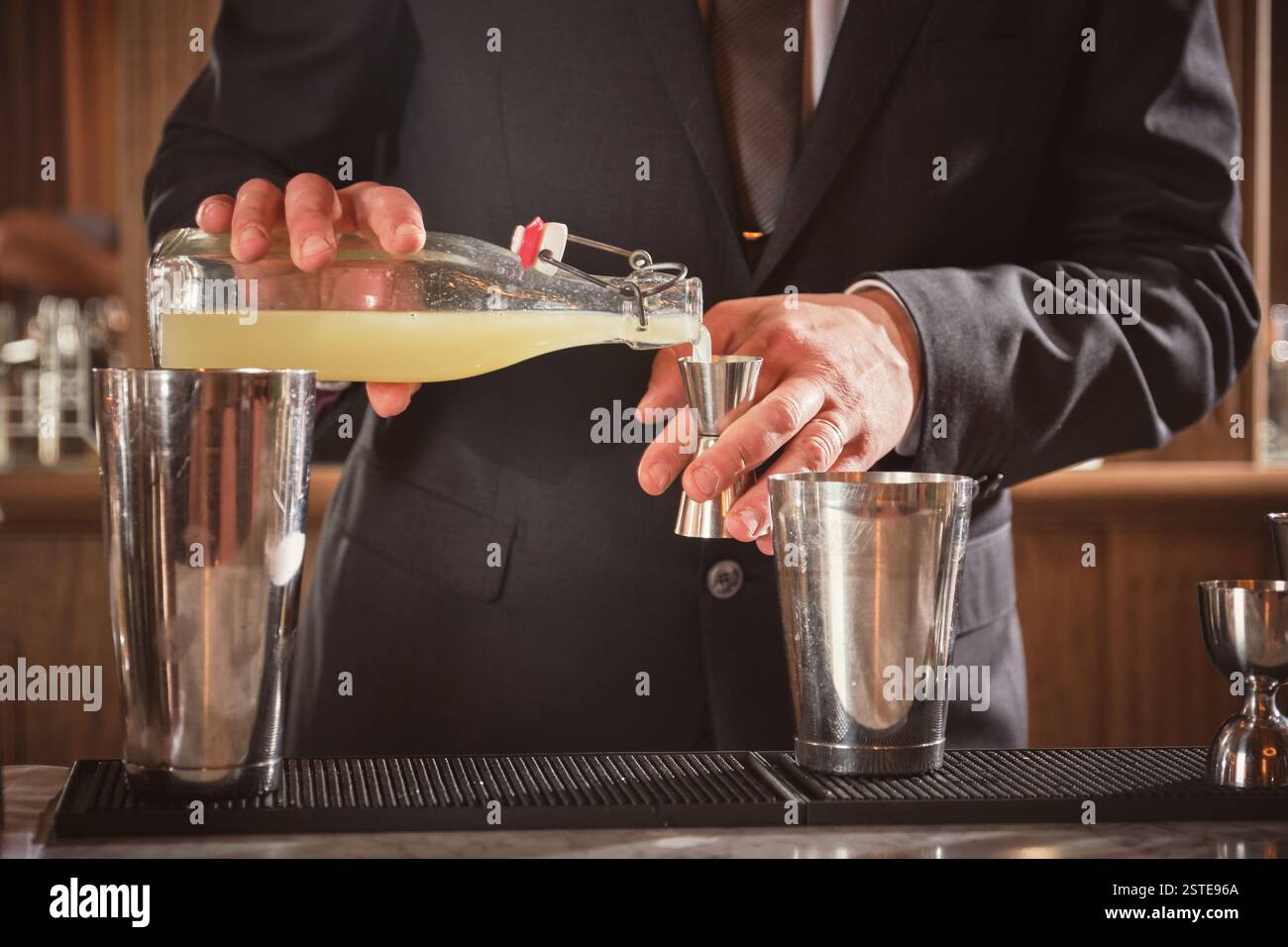 Crop anonymous male barkeeper in black suit pouring alcohol in cocktail measuring cup from ...