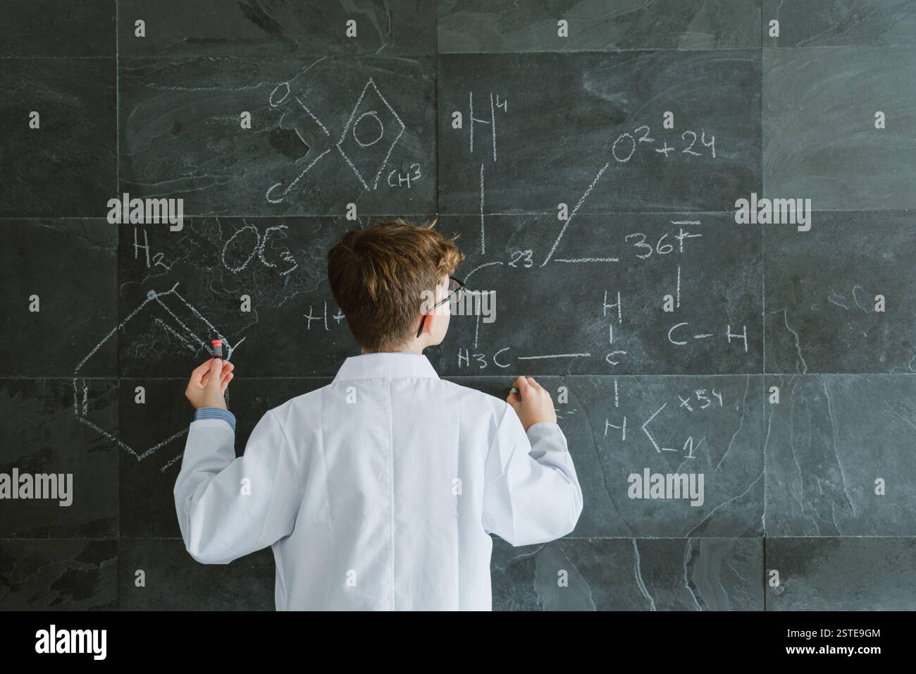 Back view of schoolboy in eyeglasses and white uniform standing while ...