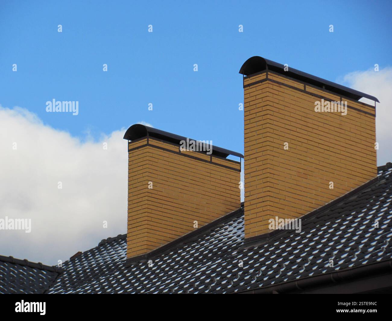 Two tall, rectangular chimneys sit atop a house with a tiled roof ...