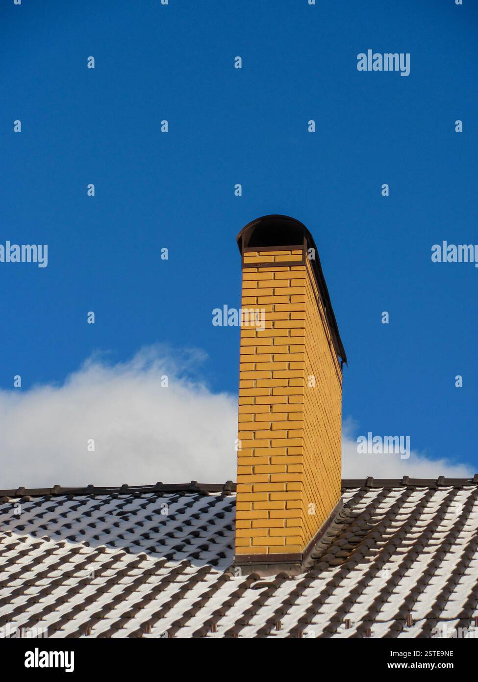 A tall yellow chimney rises above a roof with white tiles, set against ...