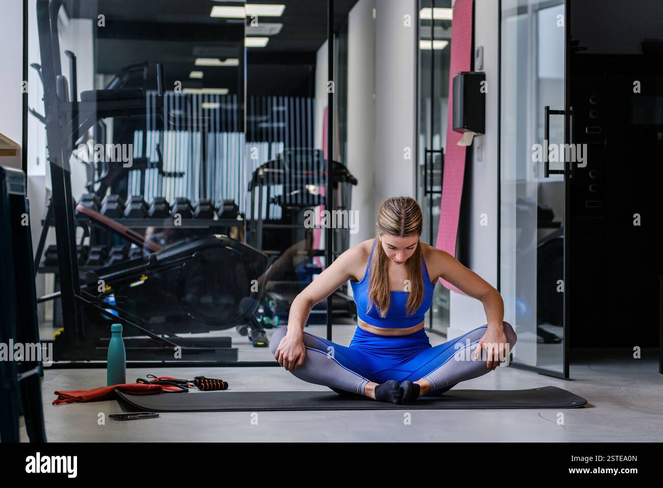 An athlete in blue performs a seated stretch on a mat, concentrating on ...