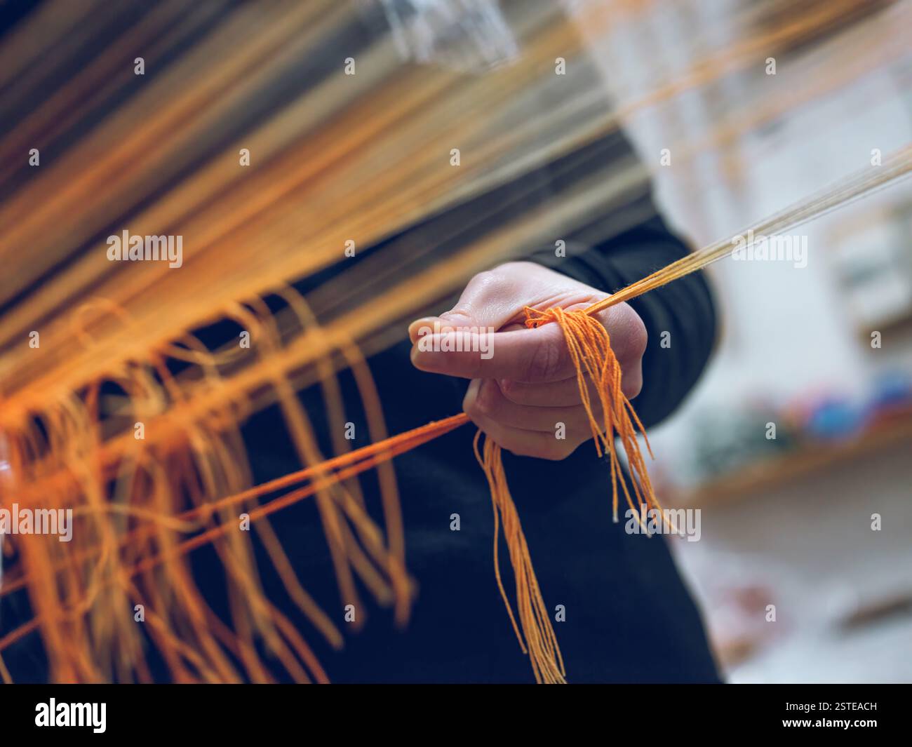 A cropped image of a worker's hand skillfully managing orange yarns in ...
