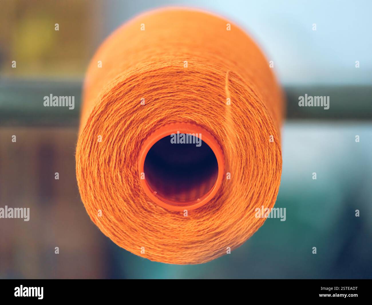 A detailed close-up of a vibrant orange yarn spool in a textile ...