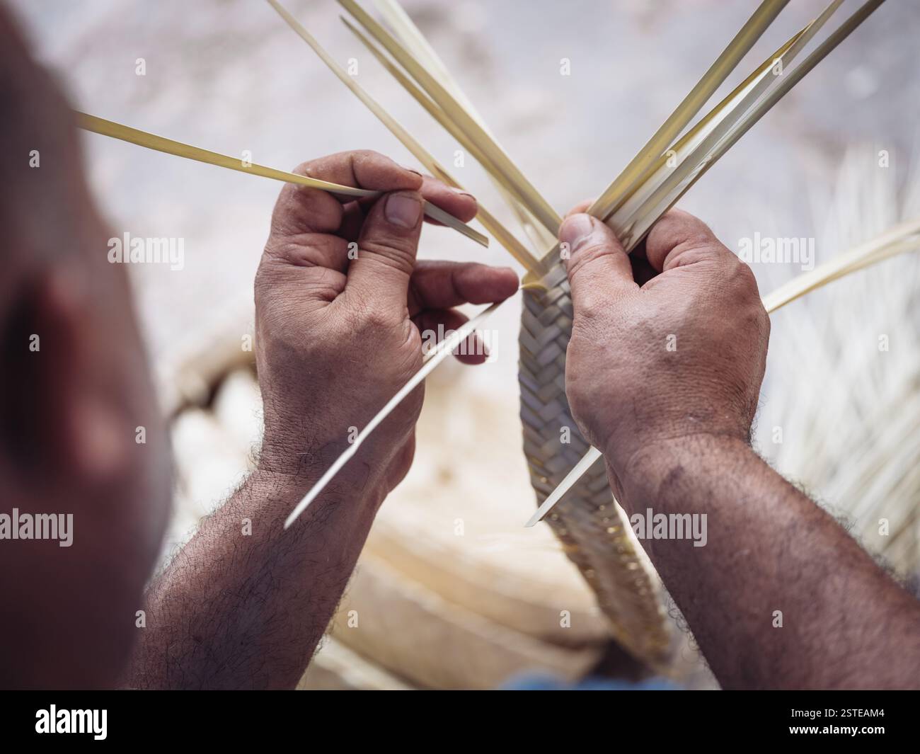 A detailed view of aged, skilled hands weaving a traditional basket ...