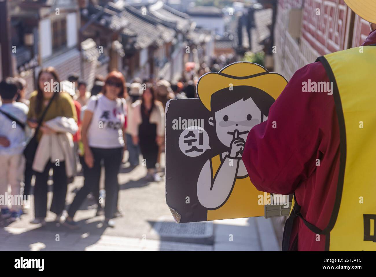 A man holding a yellow sign reminds visitors to keep quiet in Bukchon ...
