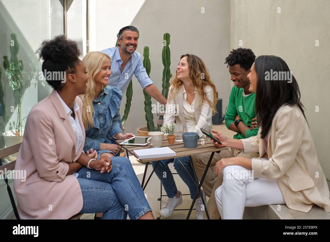 Group of multiracial coworkers gathering at wooden table on terrace ...