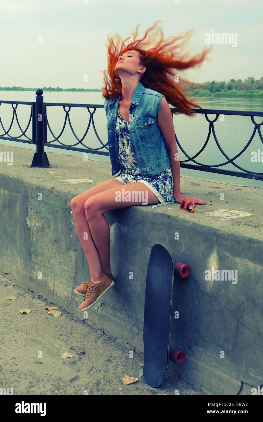 Young women sitting with her skate board on concrete street parapet ...