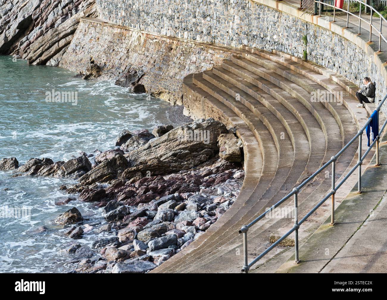A lone person sits on the steps at Beacon Cove, Torquay, Devon, England ...