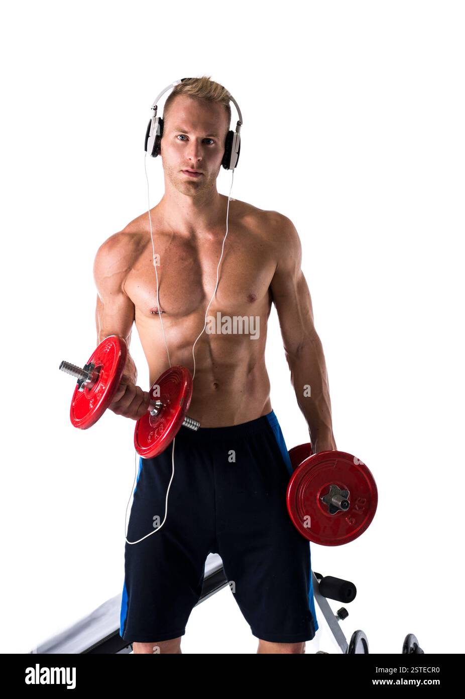 Muscular young man lifting weights and listening to music in headphones ...