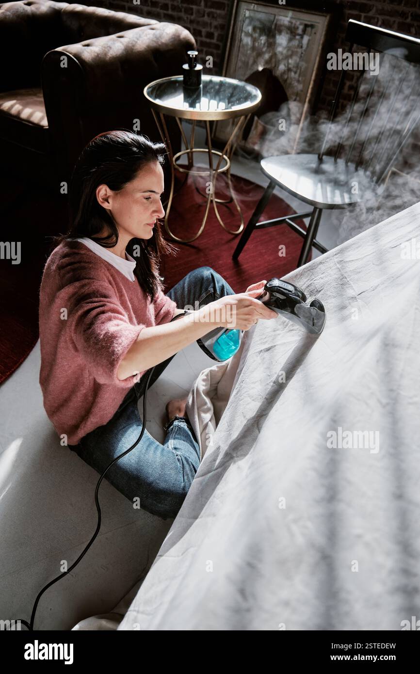 A woman uses a steam iron to gently smooth a tablecloth, creating a ...