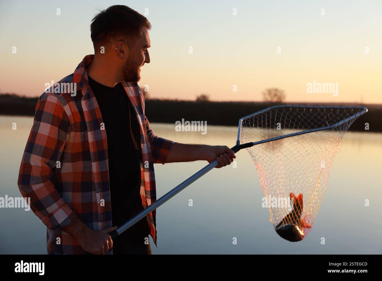 Fisherman holding fishing net with catch at riverside Stock Photo - Alamy
