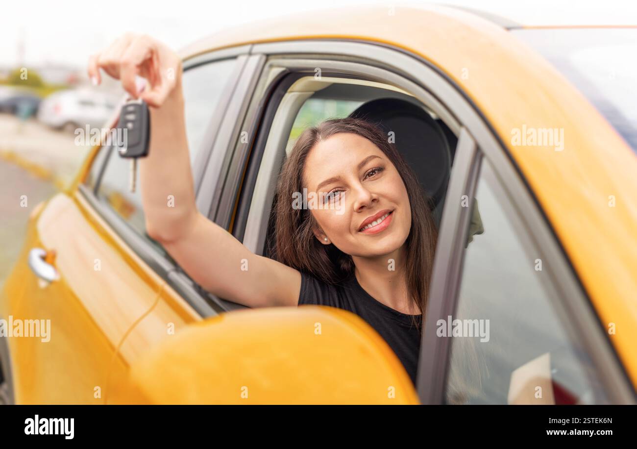 Woman with bright smile sits in the drivers seat of a yellow car ...