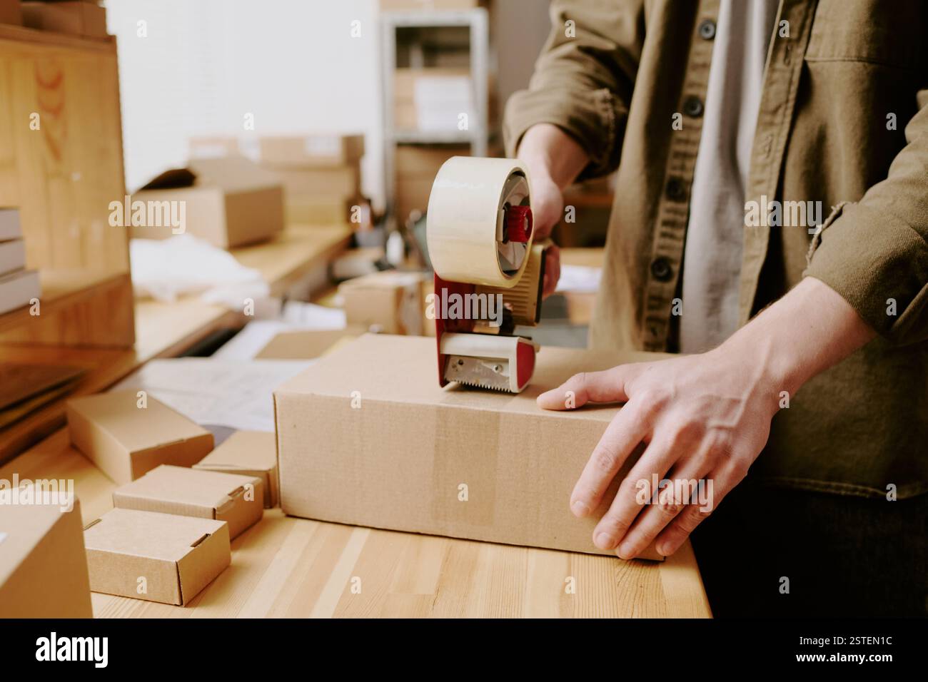 Person sealing cardboard boxes with tape dispenser in busy warehouse ...