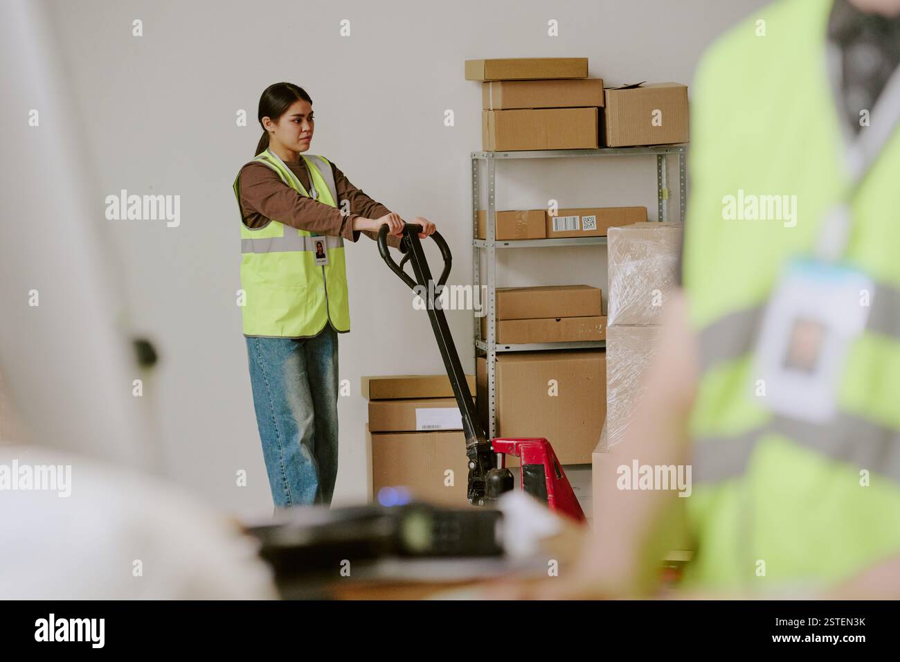 Young woman working in warehouse, moving boxes with pallet jack wearing ...
