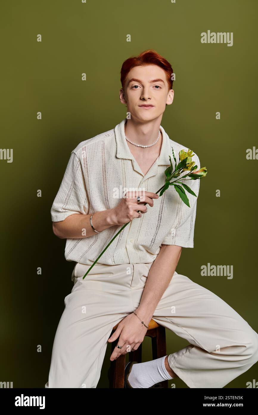 A young, handsome man sits confidently, holding a delicate flower with ...