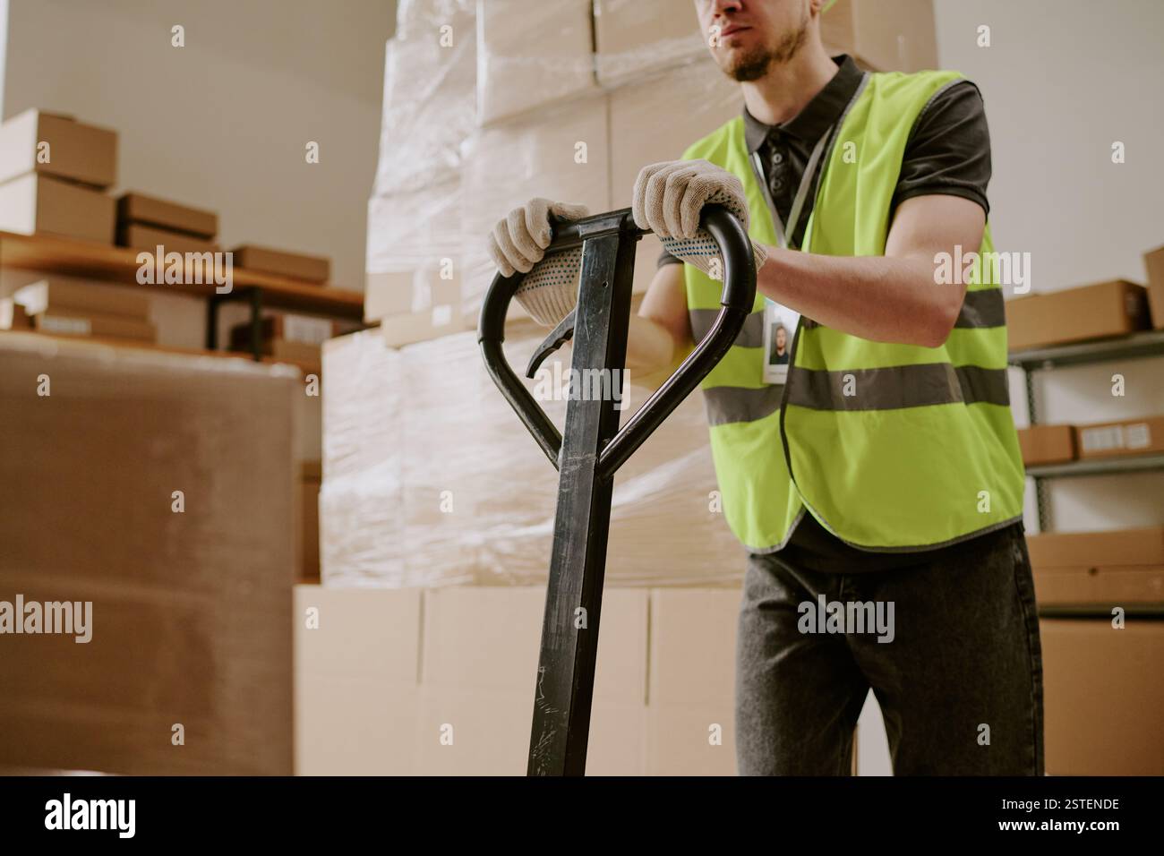 Worker in high-visibility vest operating pallet jack in warehouse ...